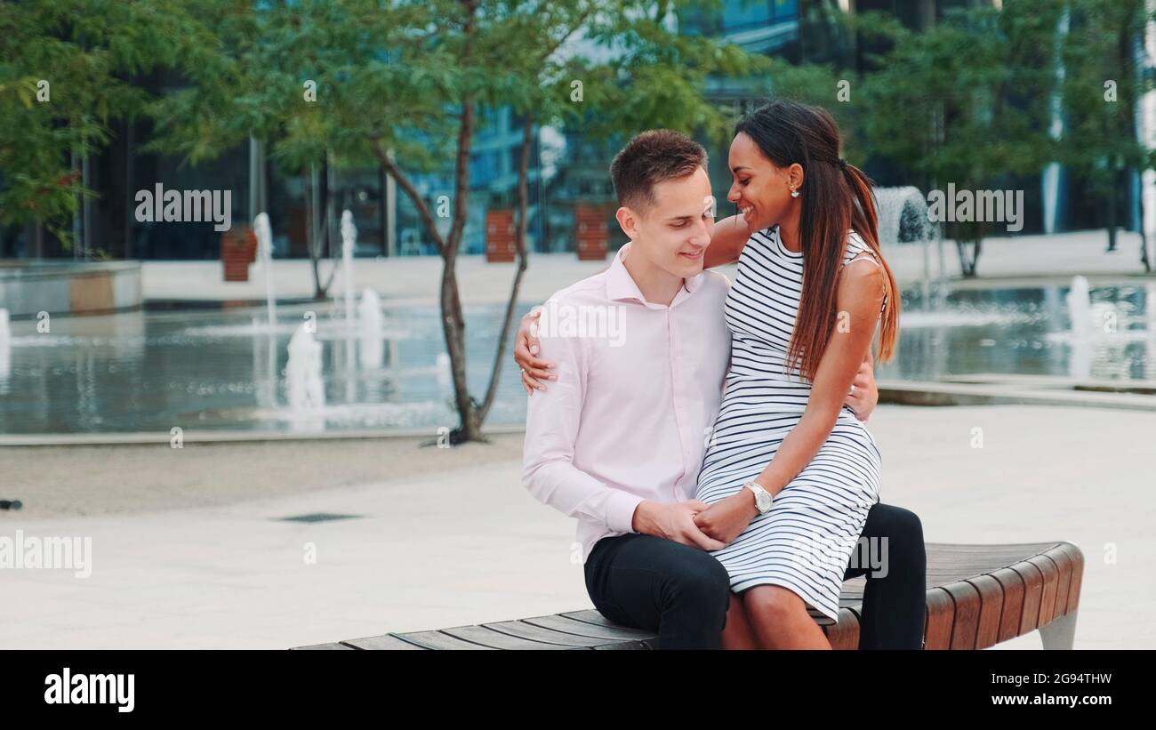 Two mixed-race lovers sitting on a bench and kissing. They having a ...