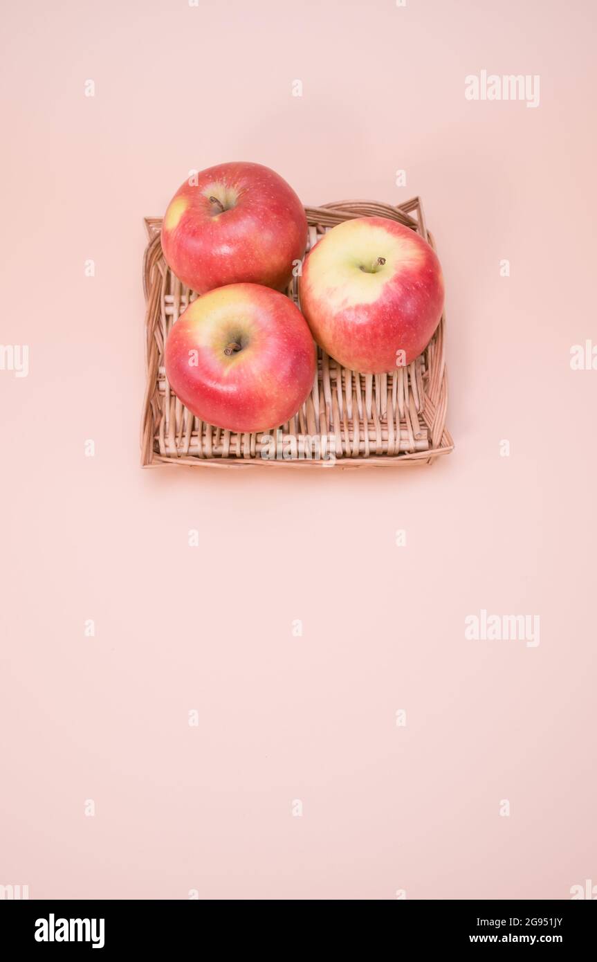 Vertical of fresh apples on a woven tray isolated on a pink background ...