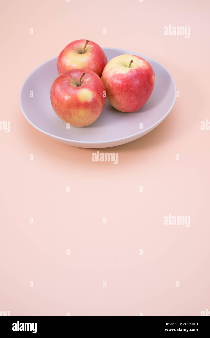 Vertical of fresh apples on a round plate isolated on a pink background ...