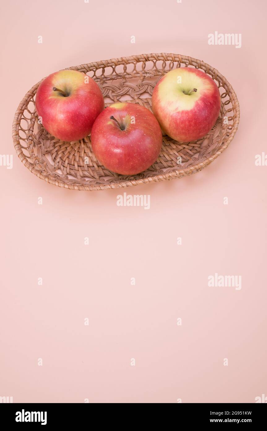 Vertical of fresh apples on a woven tray isolated on a pink background ...