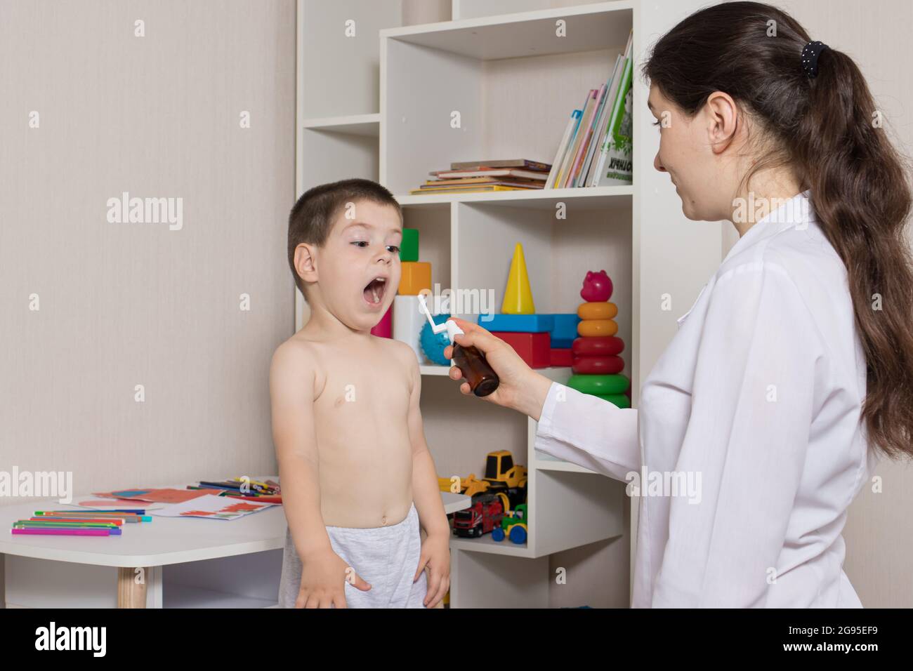 A pediatrician or nurse and a boy 3-4 years old. Throat spray ...