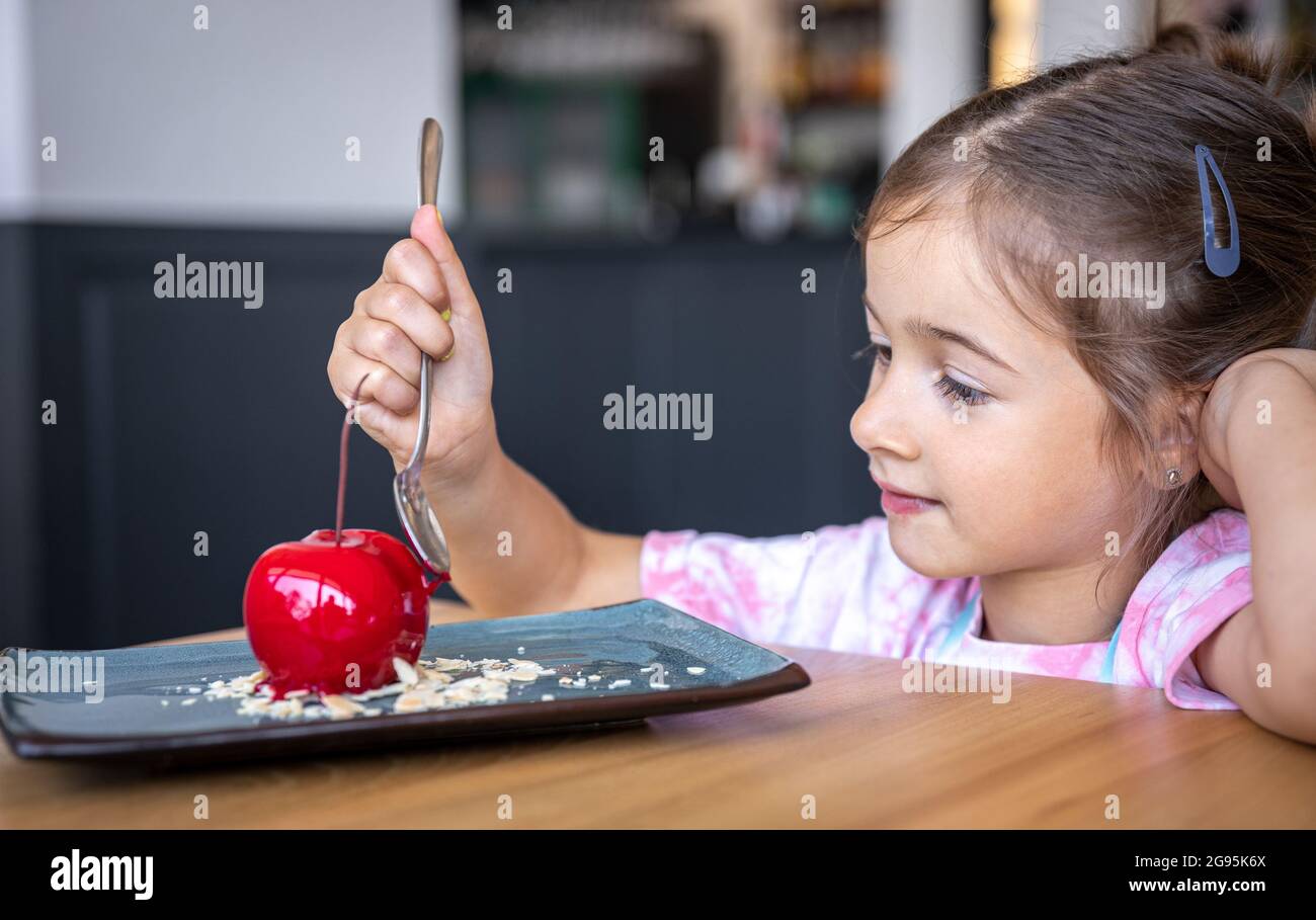 Cute little girl eating cherry-shaped chocolate mousse, french dessert ...