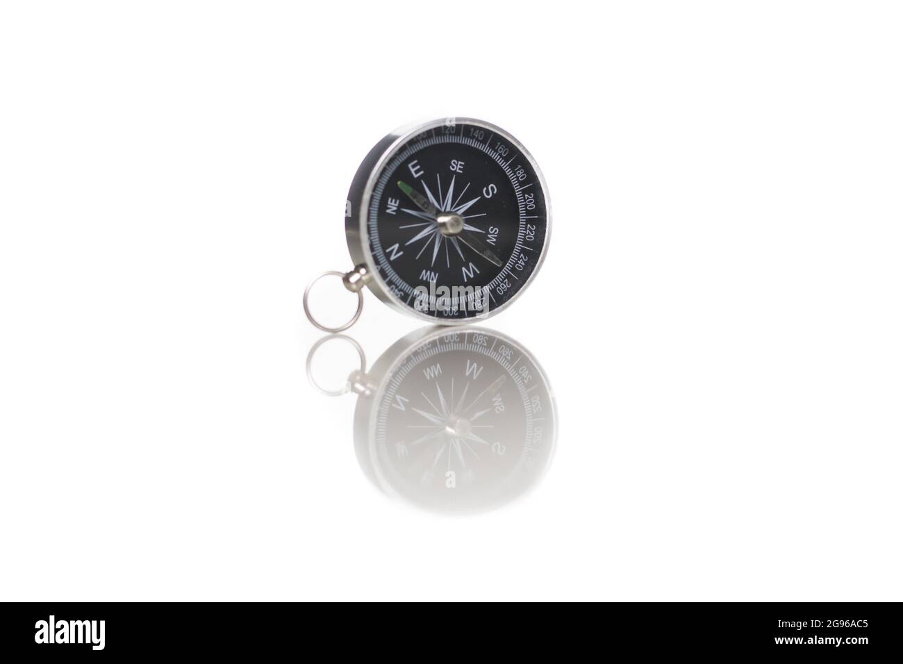 Vertical shot of a compass on a reflective surface against a white ...