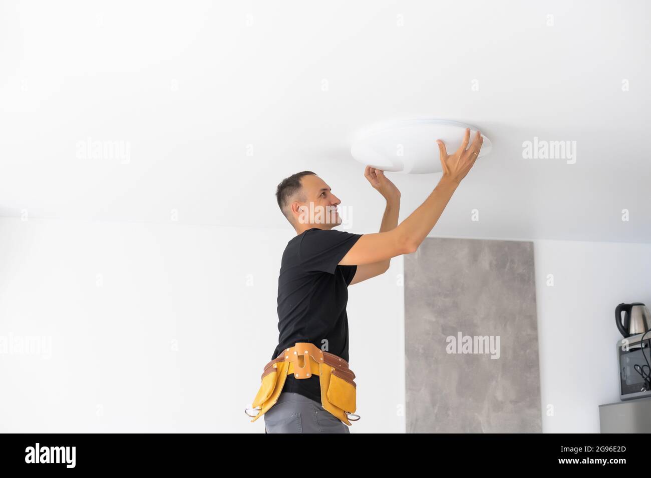 Worker repairing lamp on stretch ceiling indoors Stock Photo - Alamy