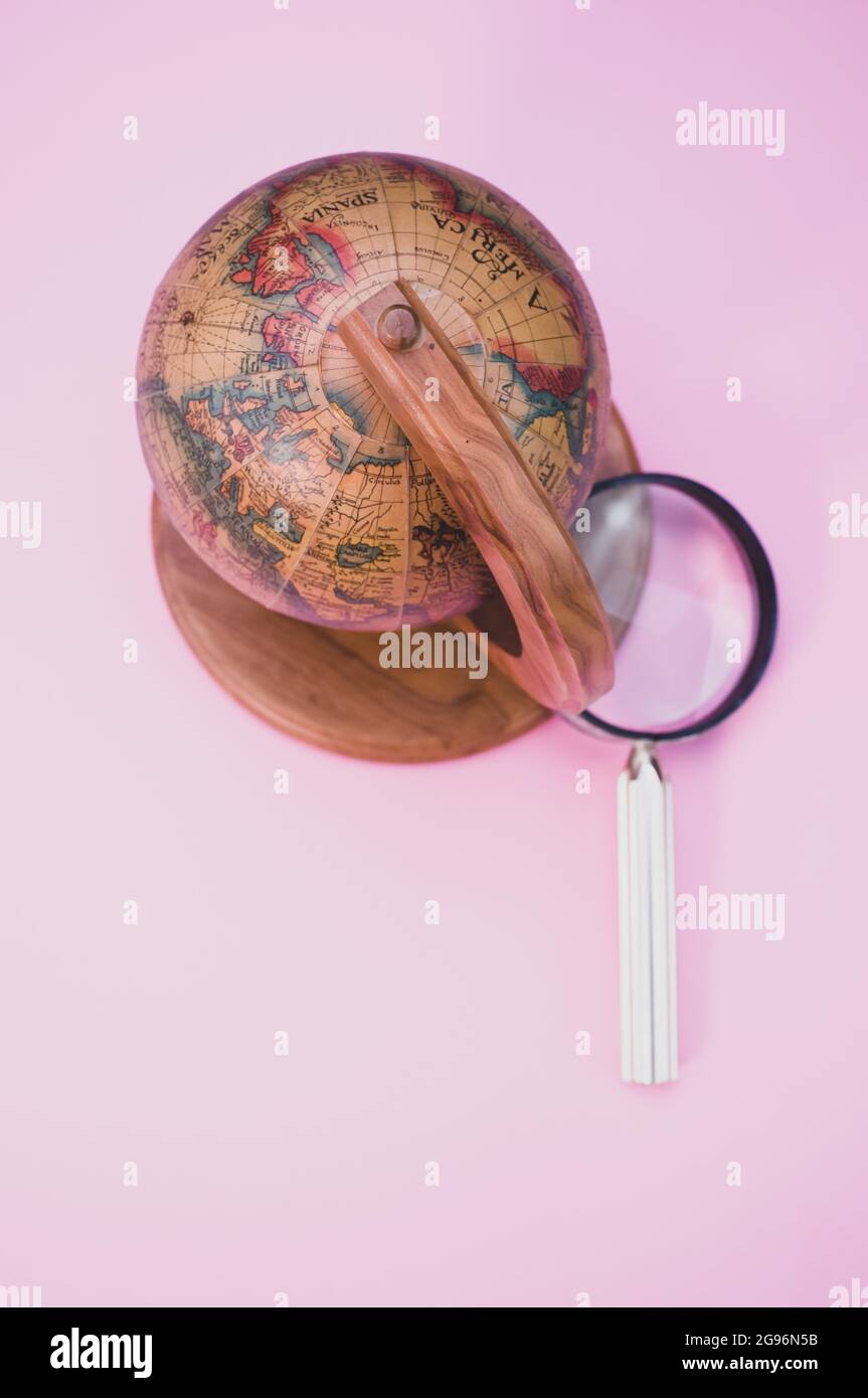 Vertical shot of wooden globe and magnifying glass isolated on pink ...