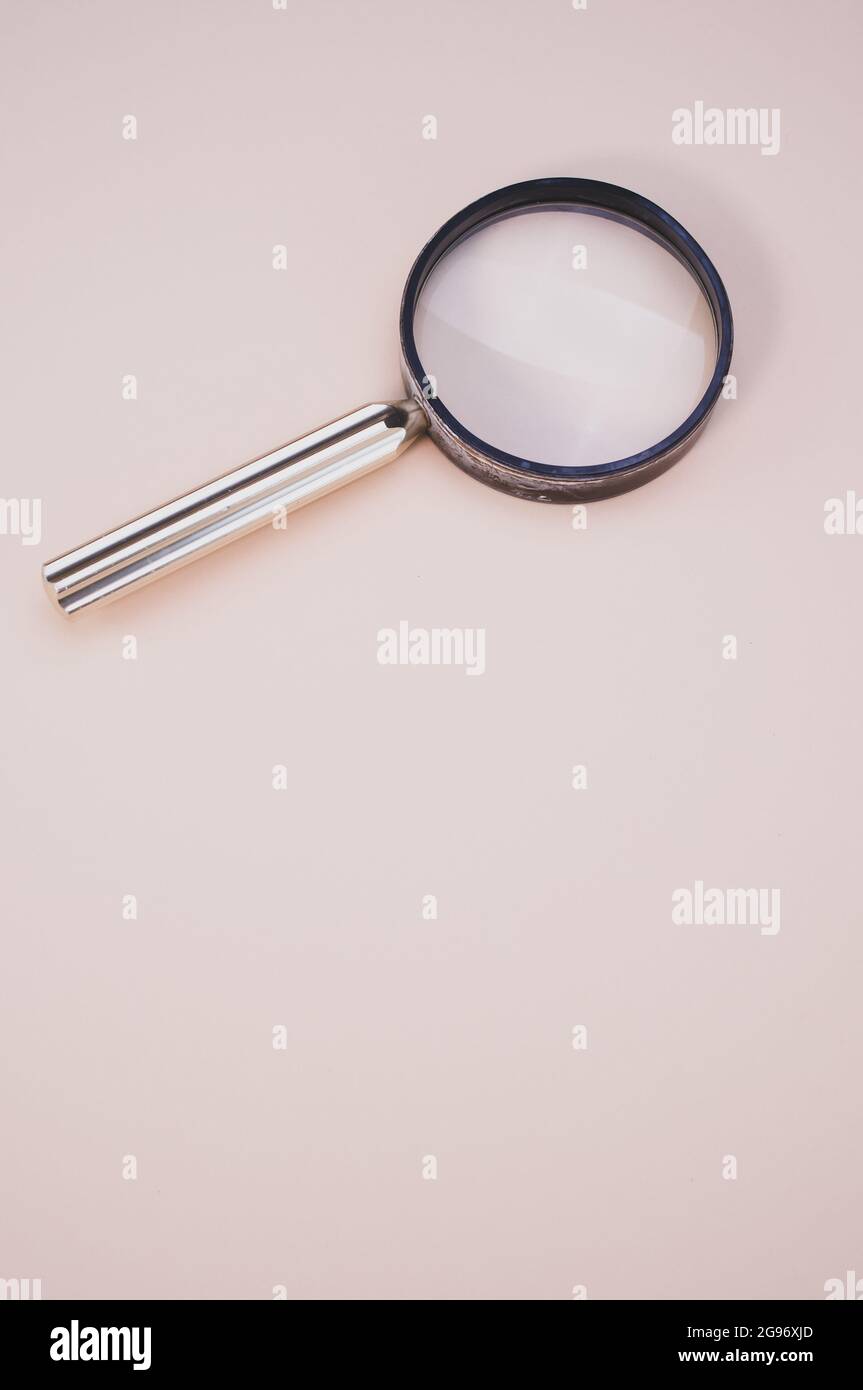 Vertical shot of magnifying glass isolated on a light cream background ...