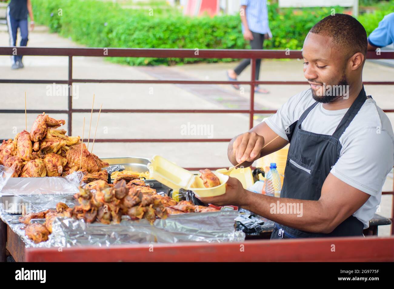 A male African barbeque and roasted chicken seller happily selling his ...