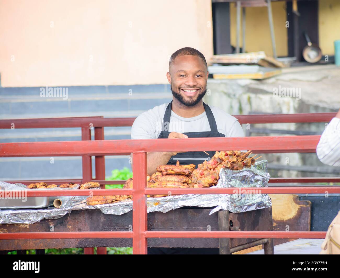 A male African barbeque and roasted chicken seller happily selling his ...