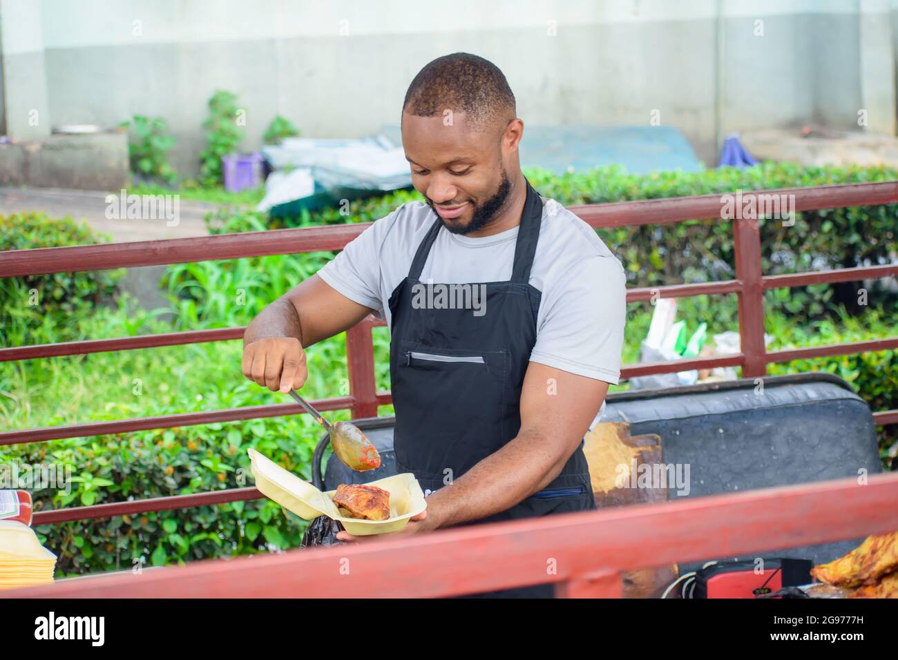A male African barbeque and roasted chicken seller happily selling his ...