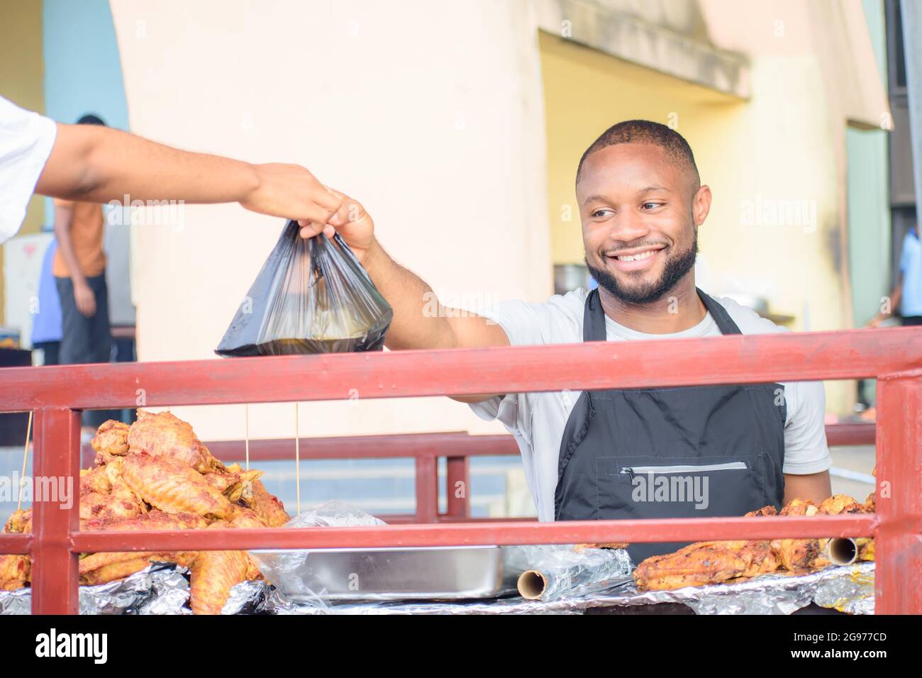 A male African barbeque and roasted chicken seller happily selling his ...