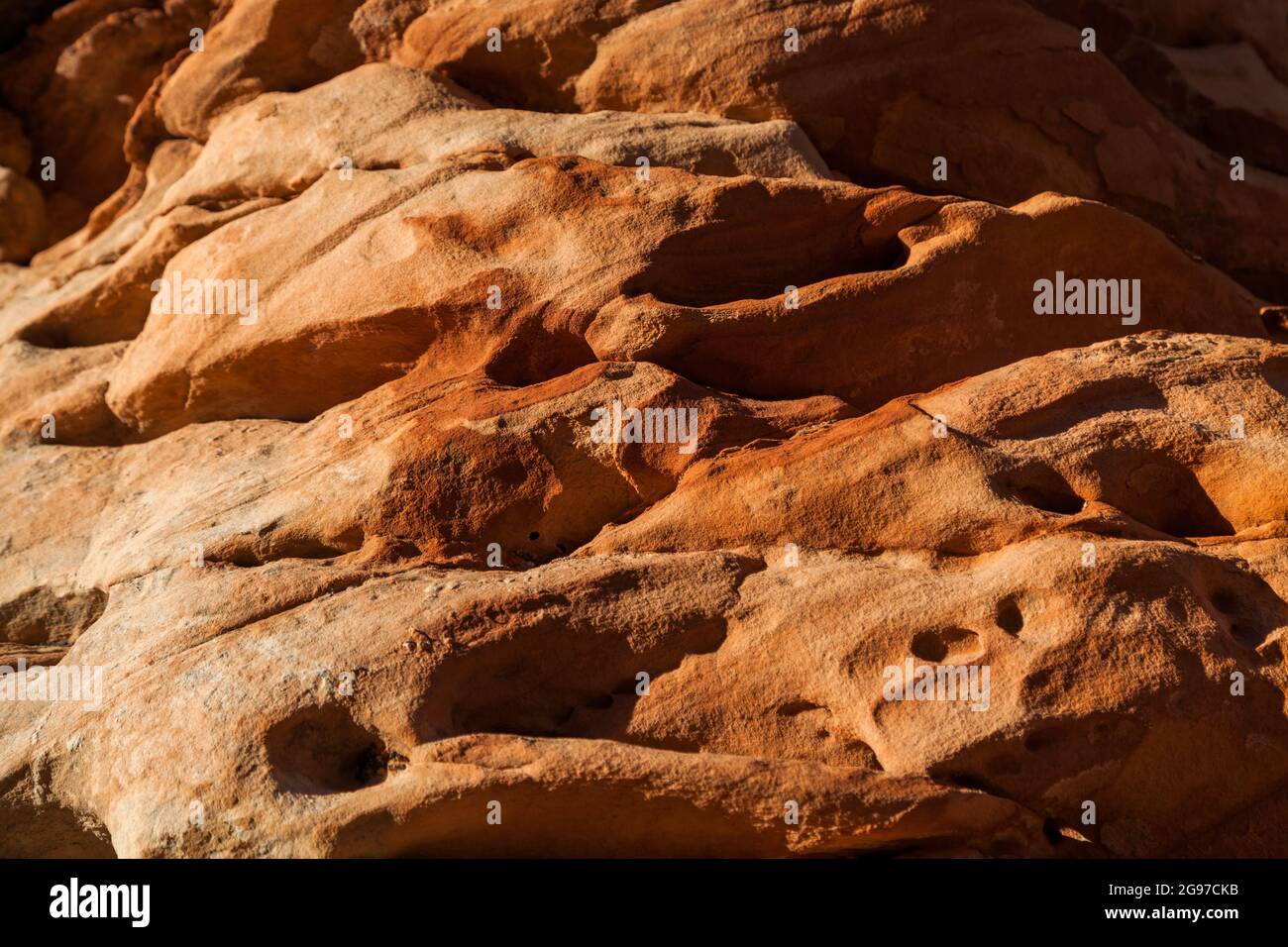Eroded red sandstone rock with swirls, layers and holes and afternoon ...