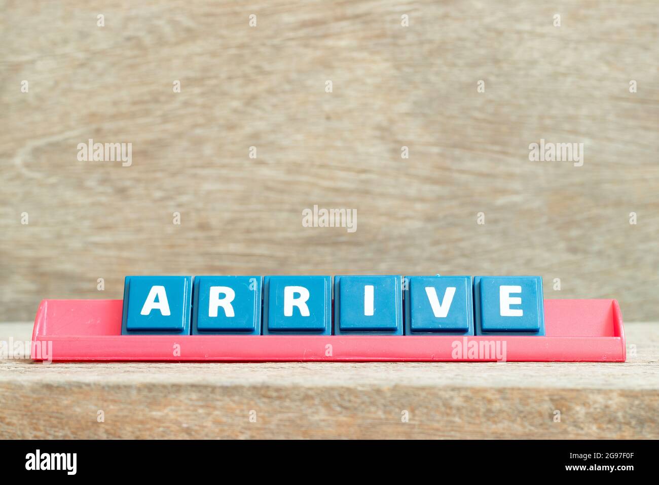 Tile alphabet letter with word arrive in red color rack on wood ...