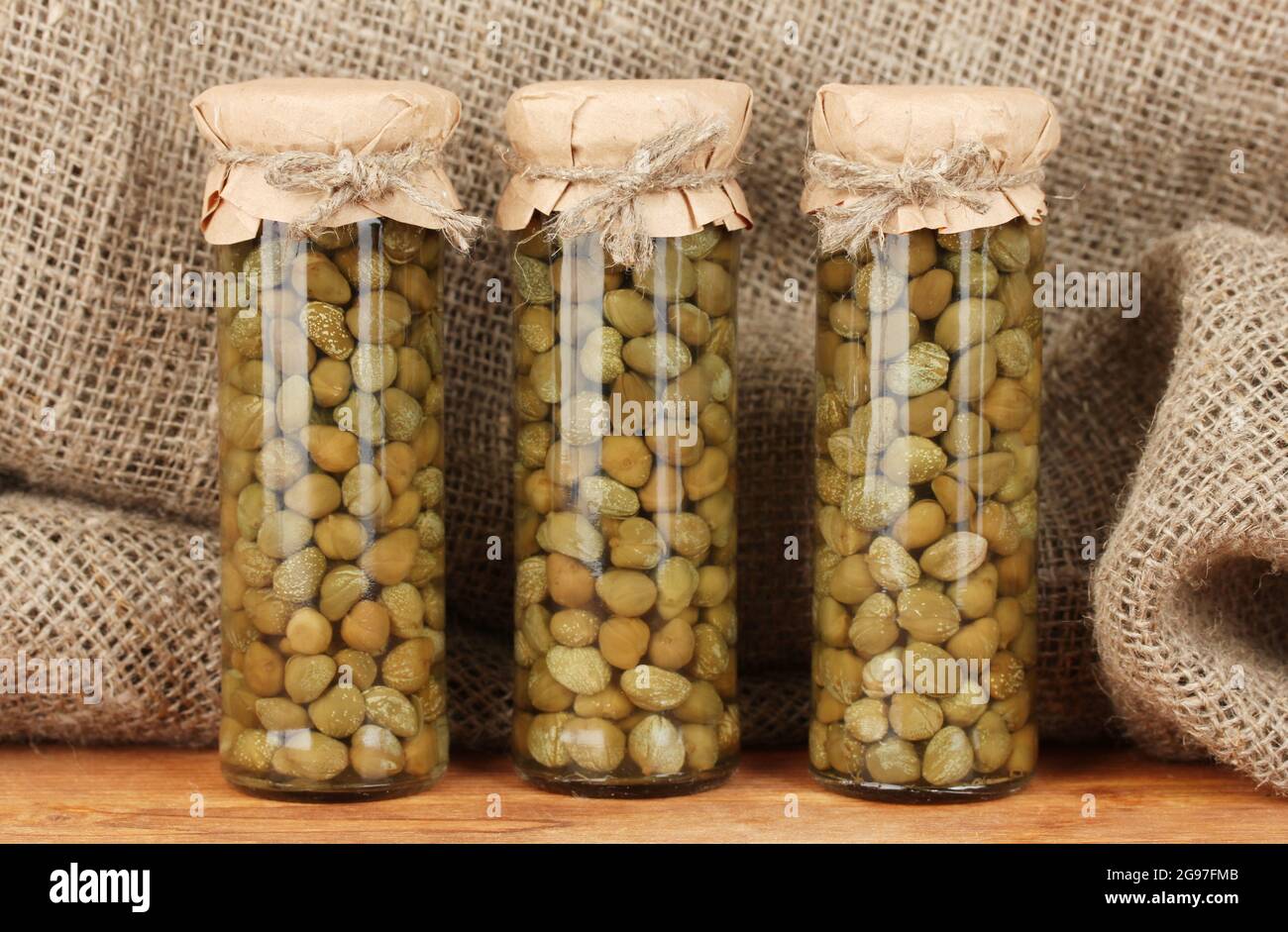 Glass jar with tinned capers on sack background close-up Stock Photo ...