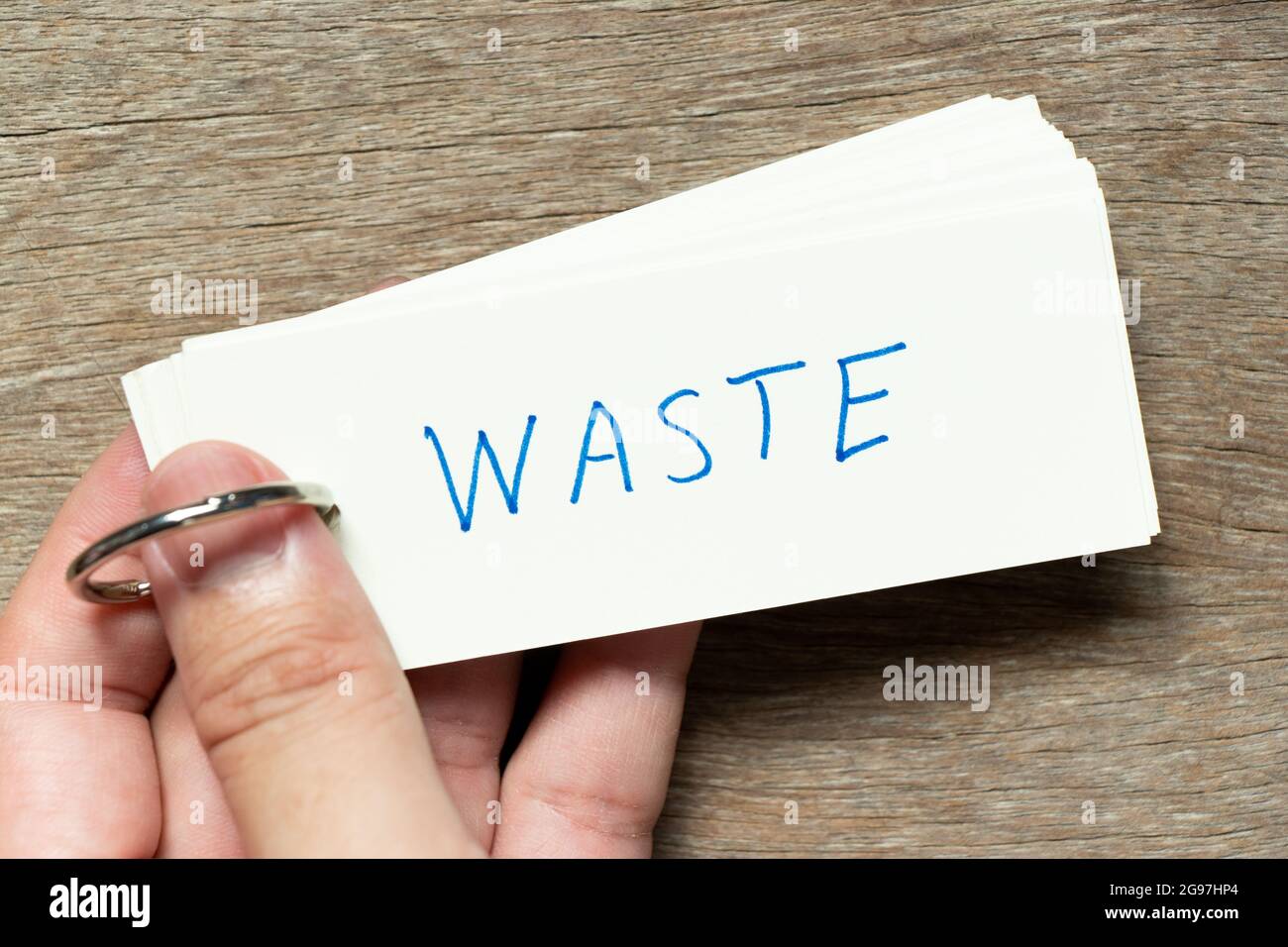 Man hold the flash card with handwriting word waste on wood background ...