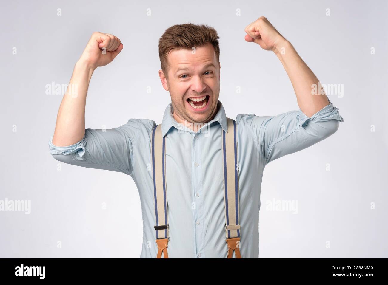 portrait of thrilled man holding fists up, against grey background ...