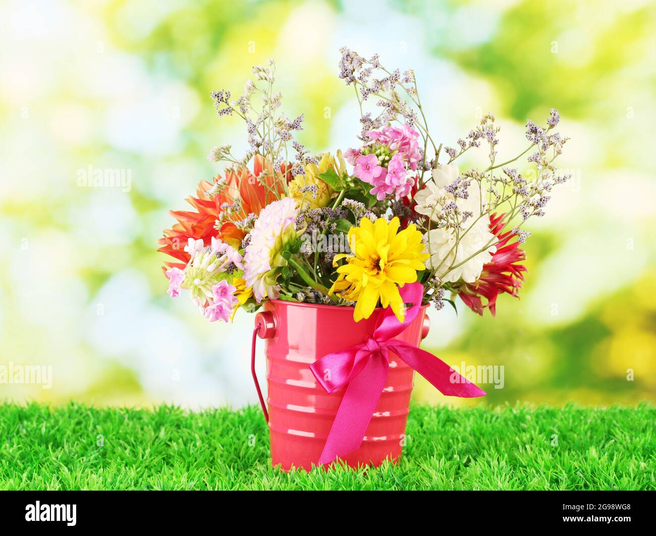 Bright pink bucket with flowers on green background Stock Photo - Alamy