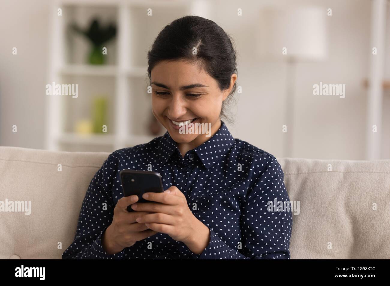 Close up smiling Indian woman using smartphone, sitting on couch Stock ...