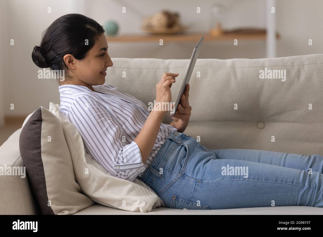 Side view smiling Indian woman using tablet, lying on couch Stock Photo ...