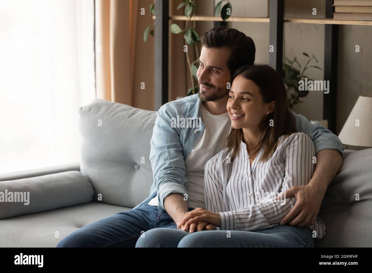 Loving couple relax on sofa cuddling daydreaming looking into distance ...