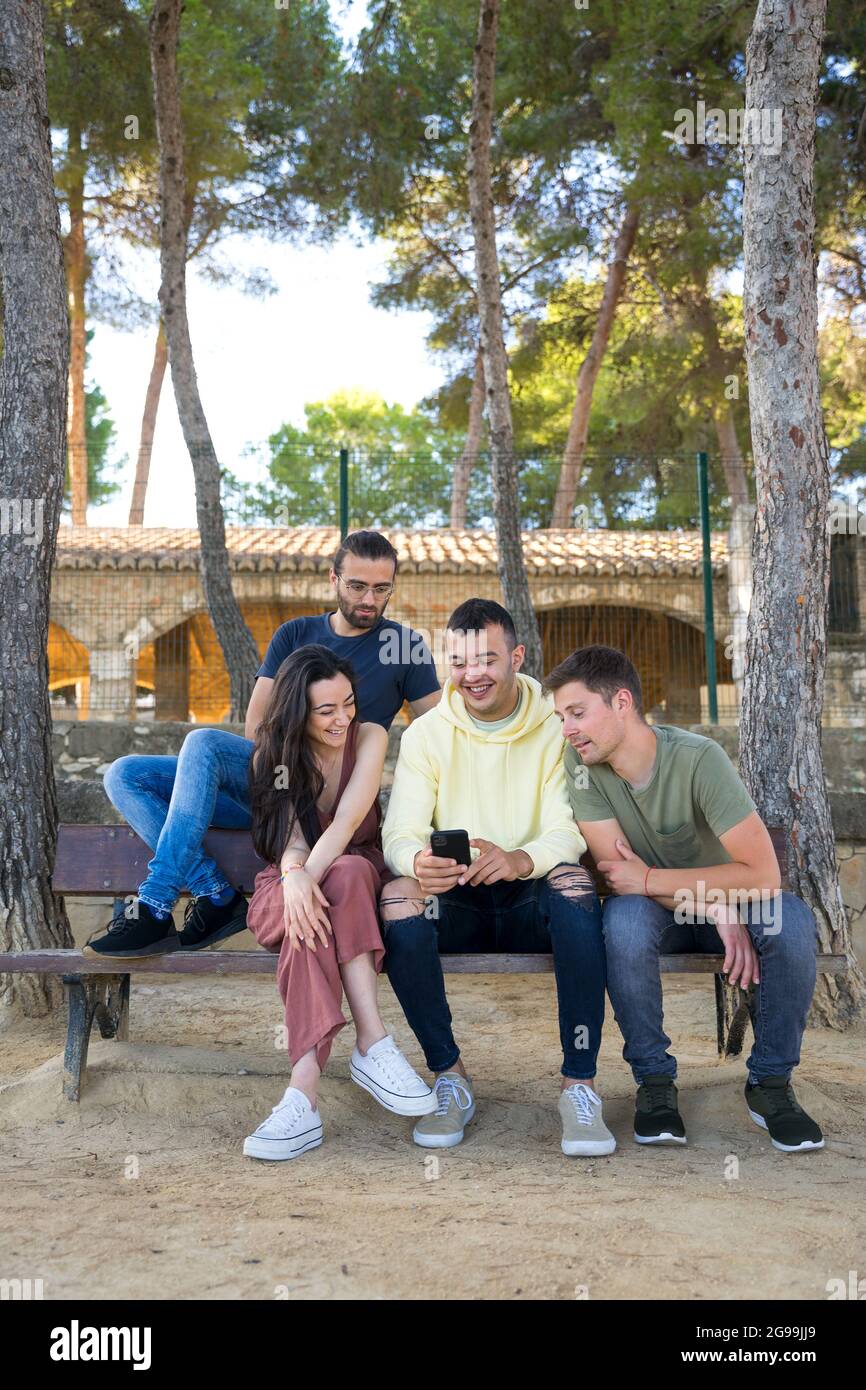 Group of friends sitting on a park bench. They are smiling while ...