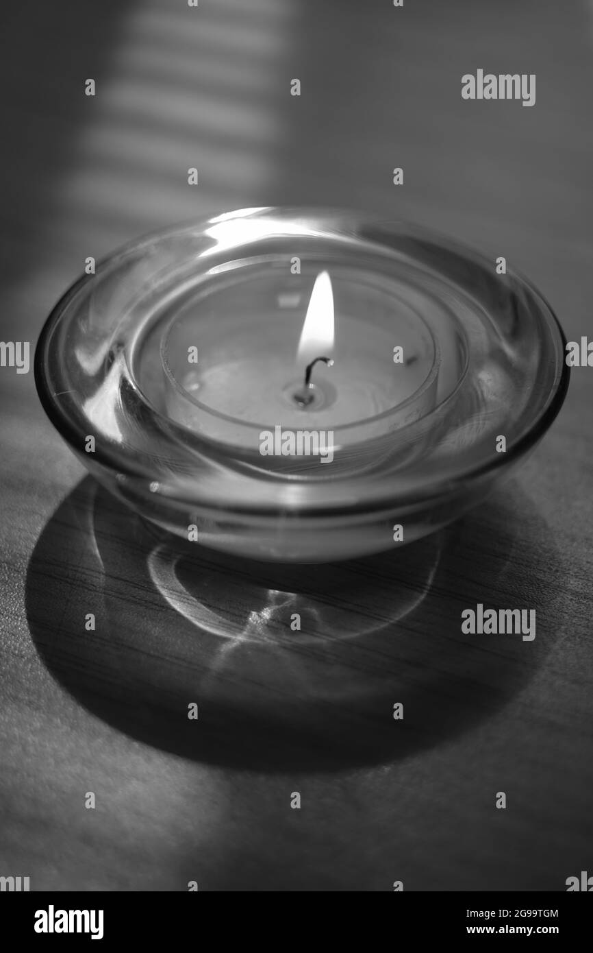 Low candle burns in a round glass candlestick on the dark table. BW ...