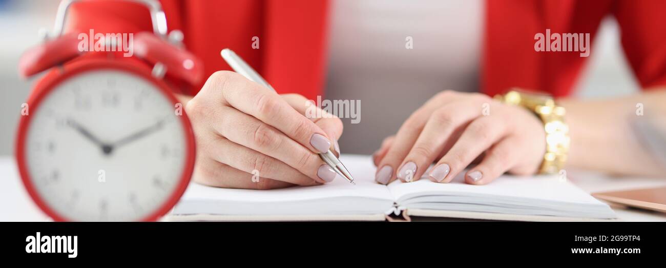 Businesswoman makes notes in documents there is an alarm clock next to ...