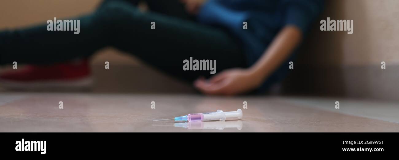 Addict sits in dark corner next to syringe with needle. Drug abuse and ...