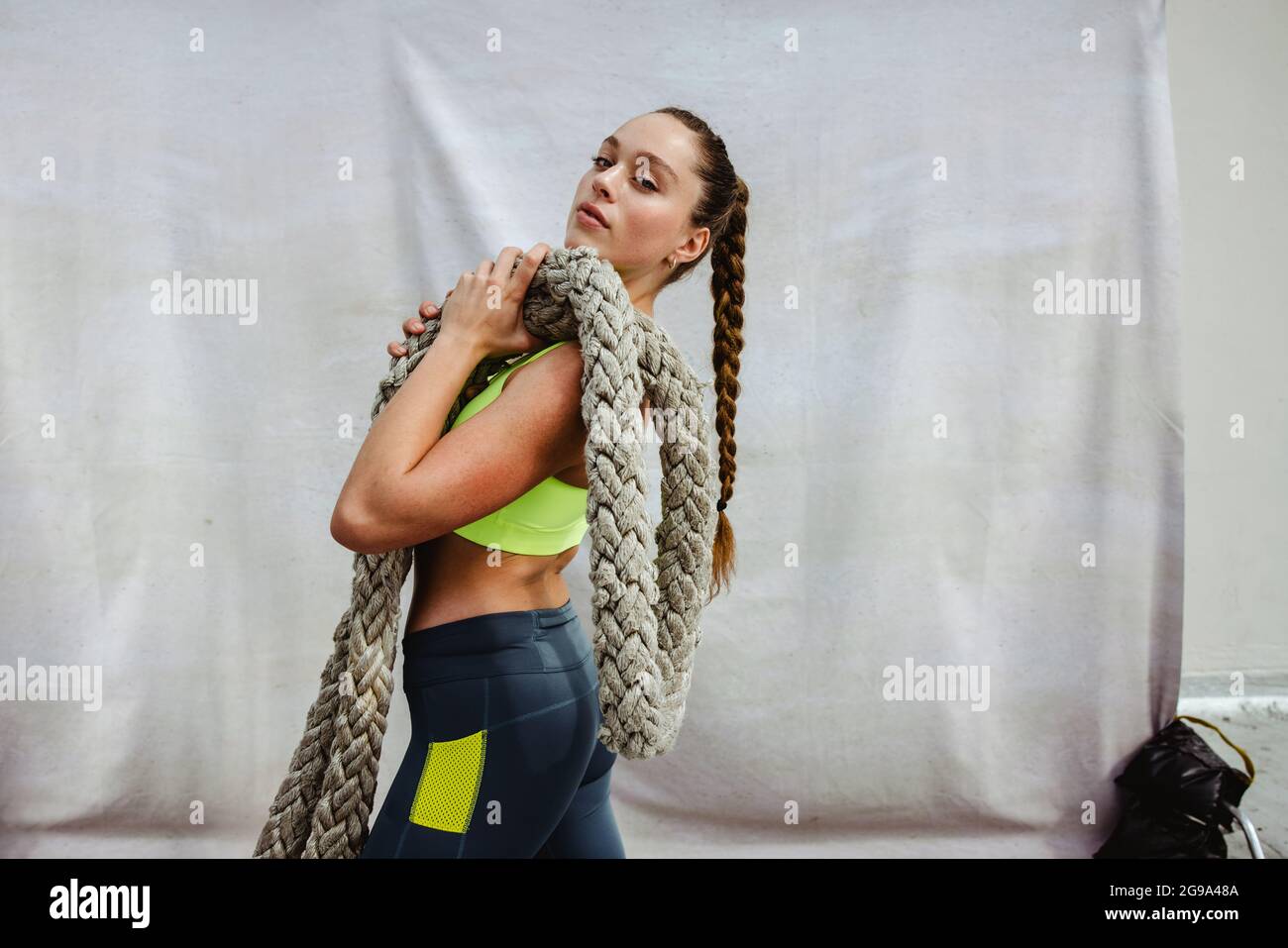 Woman in sports wear with battle rope standing on white background ...