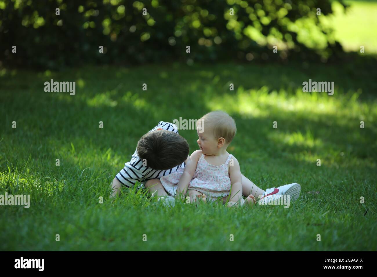 Two adorable siblings sitting on the ground in a park on a sunny day ...