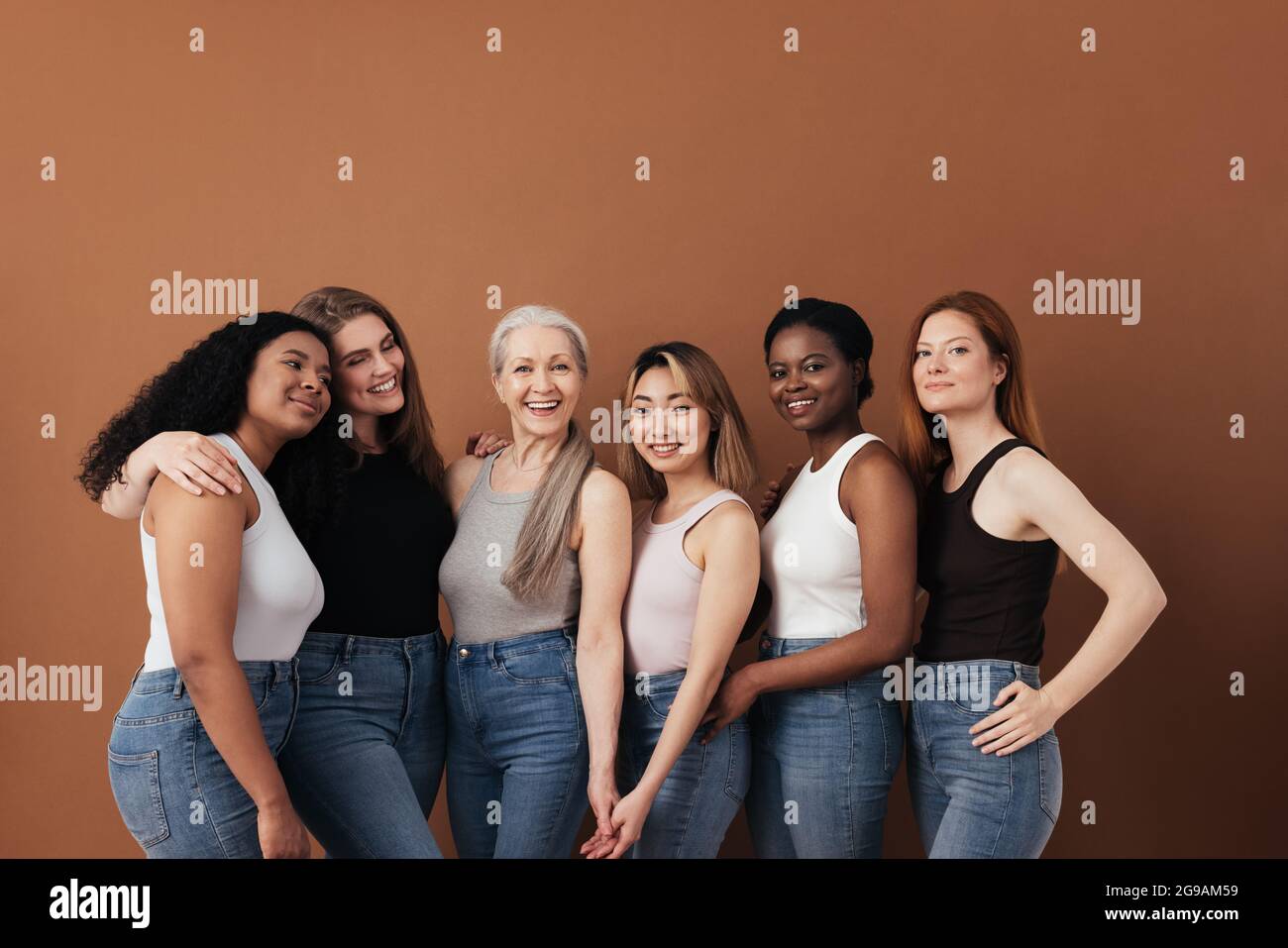 Multi-ethnic group of women of different ages posing against brown ...