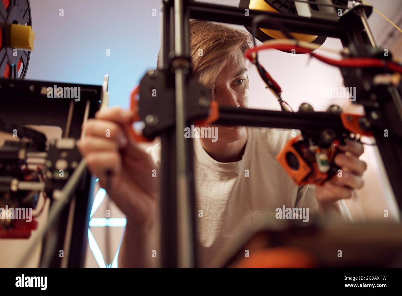 Low angle of young man fixing mechanism of 3D printer while working in ...