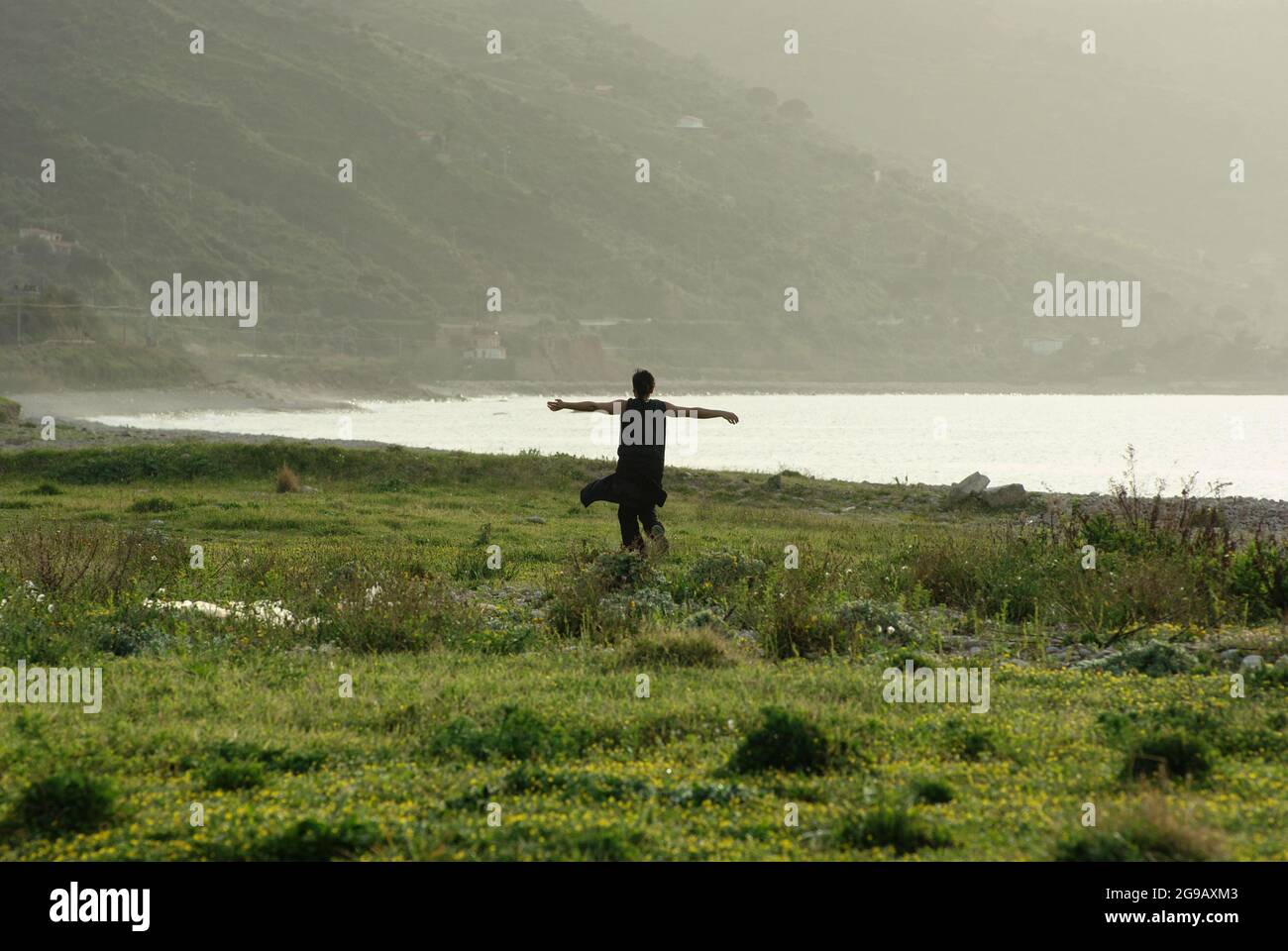 alone boy/girl running arms out across green field toward the sea in ...