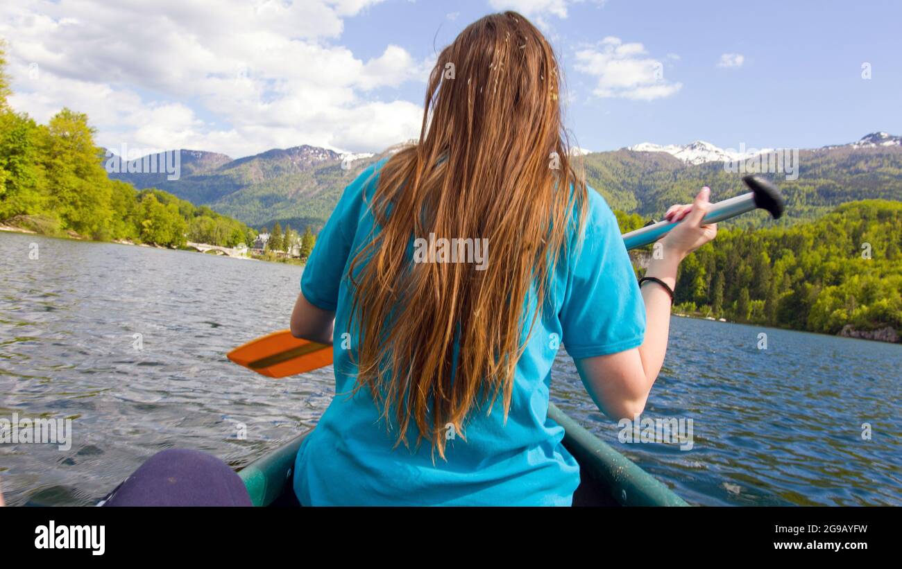 Young woman canoeing using a single-bladed paddle, traveling down a ...