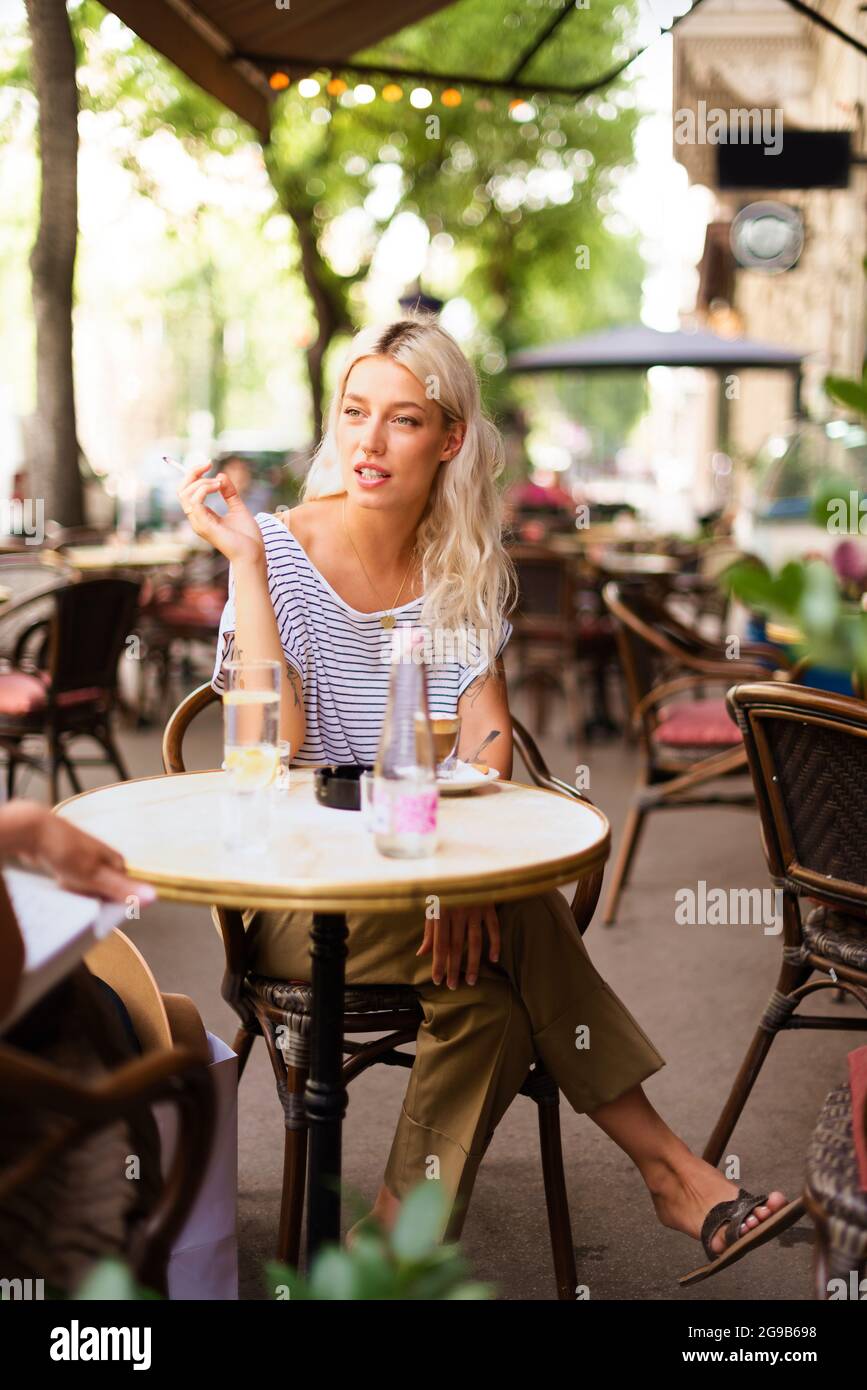 Young woman smoking a cigarette and drinking coffee while sitting ...