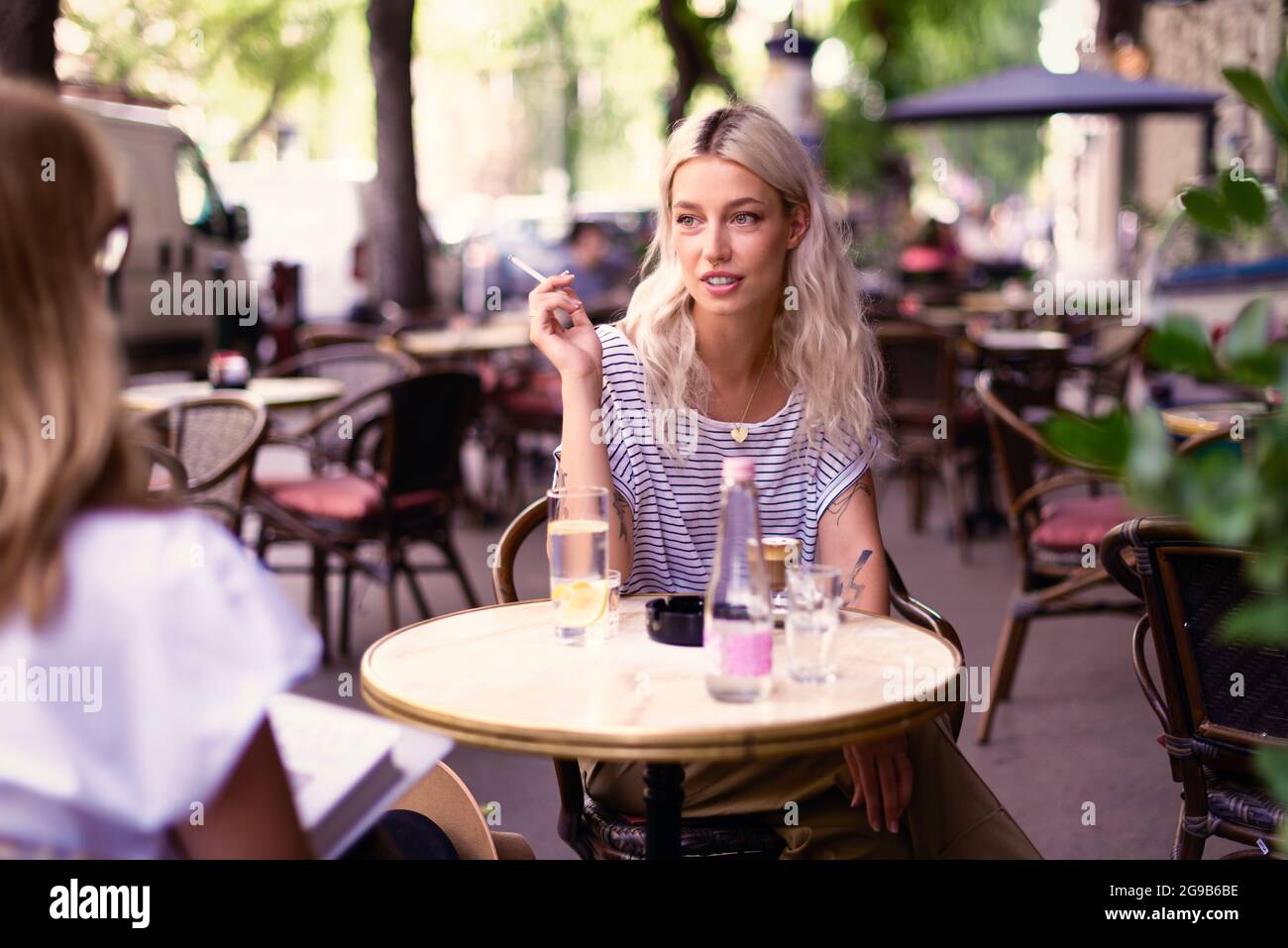 Young woman smoking a cigarette and drinking coffee while sitting ...