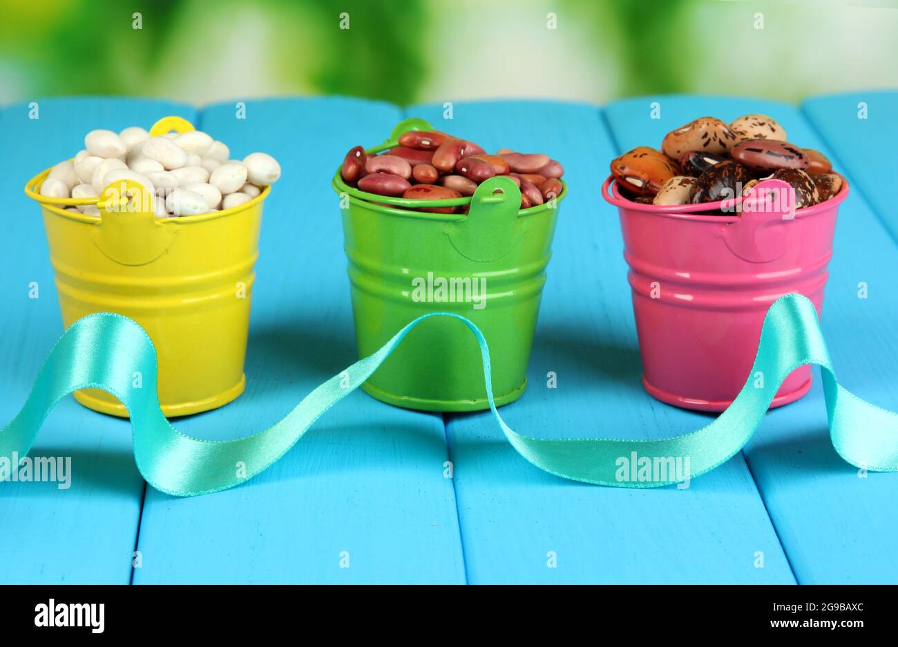 Different types of beans in colored buckets on blue wooden table on ...