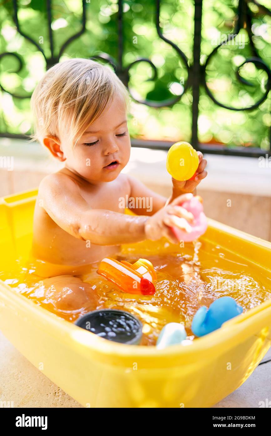 Little child sits in a basin of water and plays with toys Stock Photo ...
