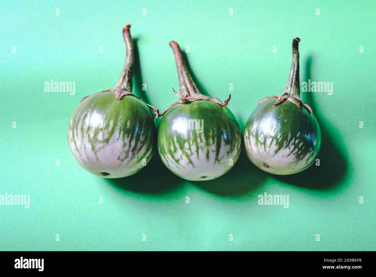 A closeup shot of fresh raw baby eggplants on a green background with a ...