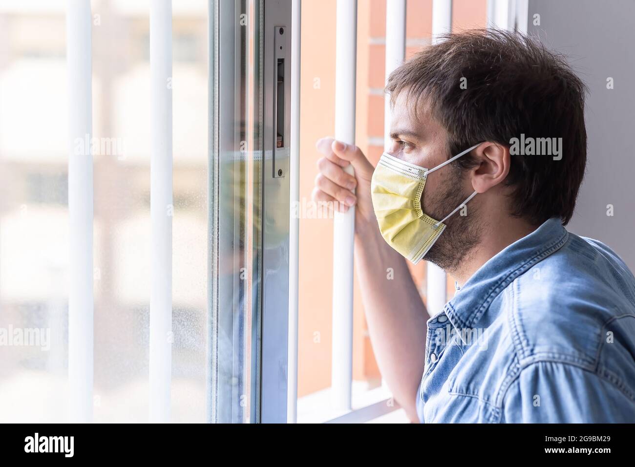 A person looking out of the window with desperation with a mask on his ...