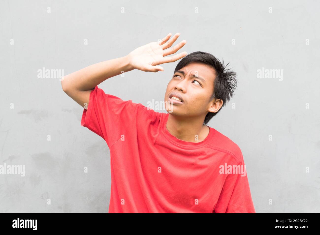 A closeup of a Southeast Asian boy holding his hand to his head ...