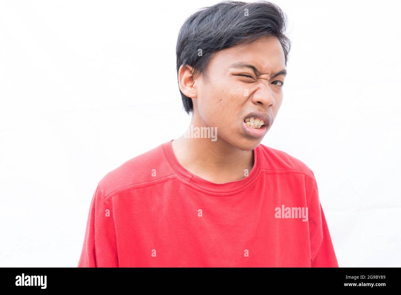 A closeup of a Southeast Asian boy grinding his teeth and winking to ...