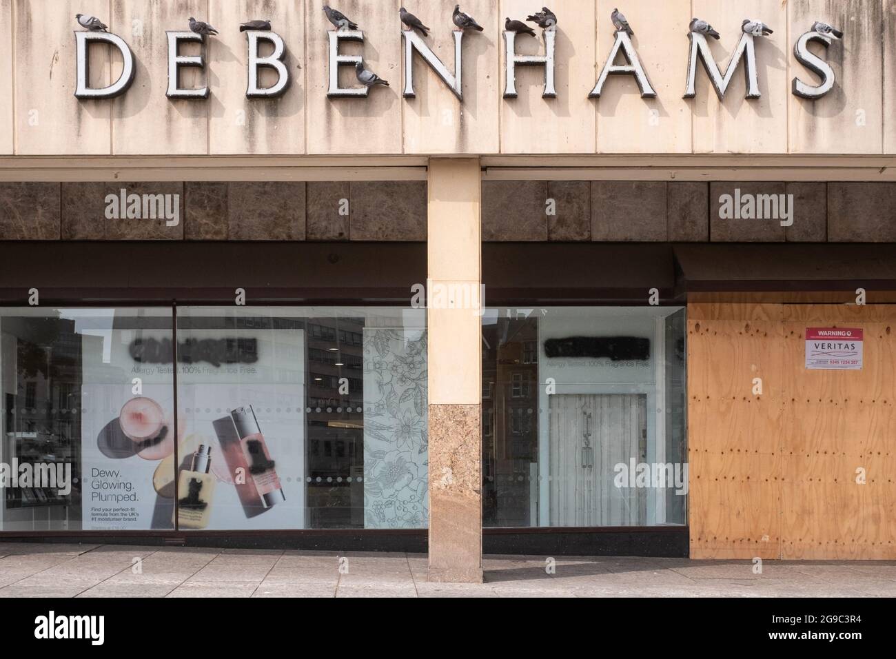 Closed and boarded up branch of Debenhams department store, with pigeons roosting on the sign ...