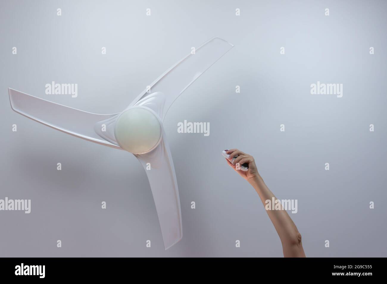 Close-up of hand holding remote control of white ceiling fan. Hand ...