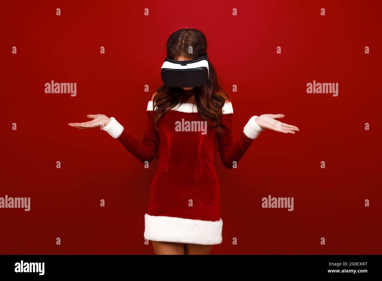 Amazed young Santa girl in Christmas dress looking in headset pointing ...