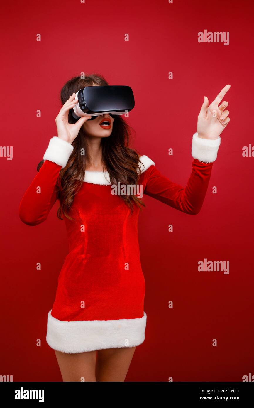 Amazed young Santa girl in Christmas dress looking in headset pointing ...