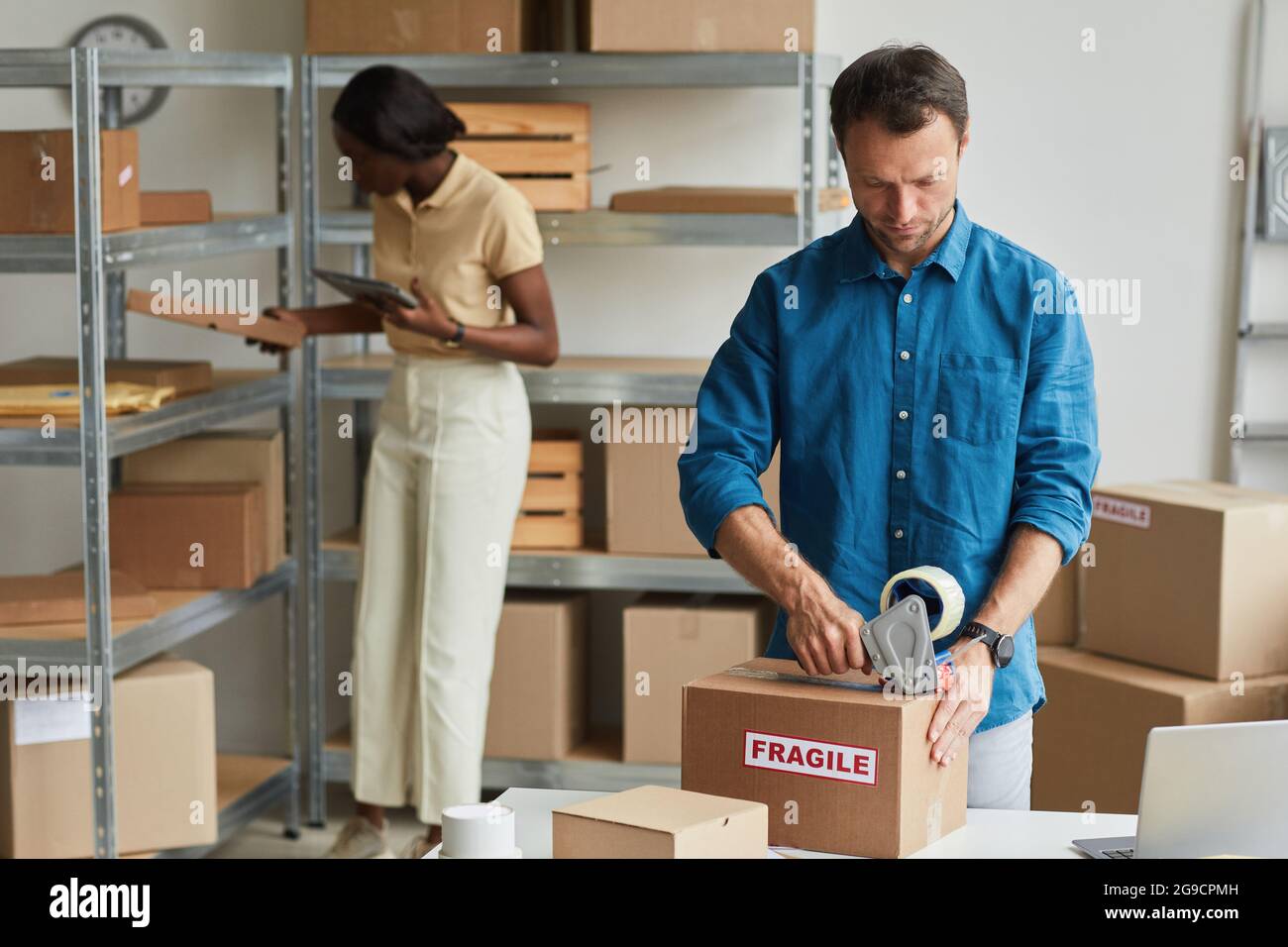 Portrait of young man packing boxes with Fragile sticker at warehouse ...
