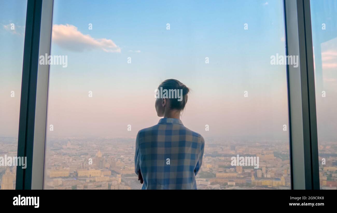 Back view of pensive woman looking at cityscape through window of ...