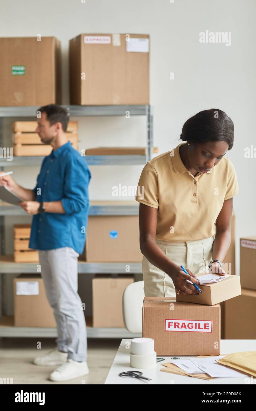 Vertical portrait of African-American woman packing boxes at warehouse ...