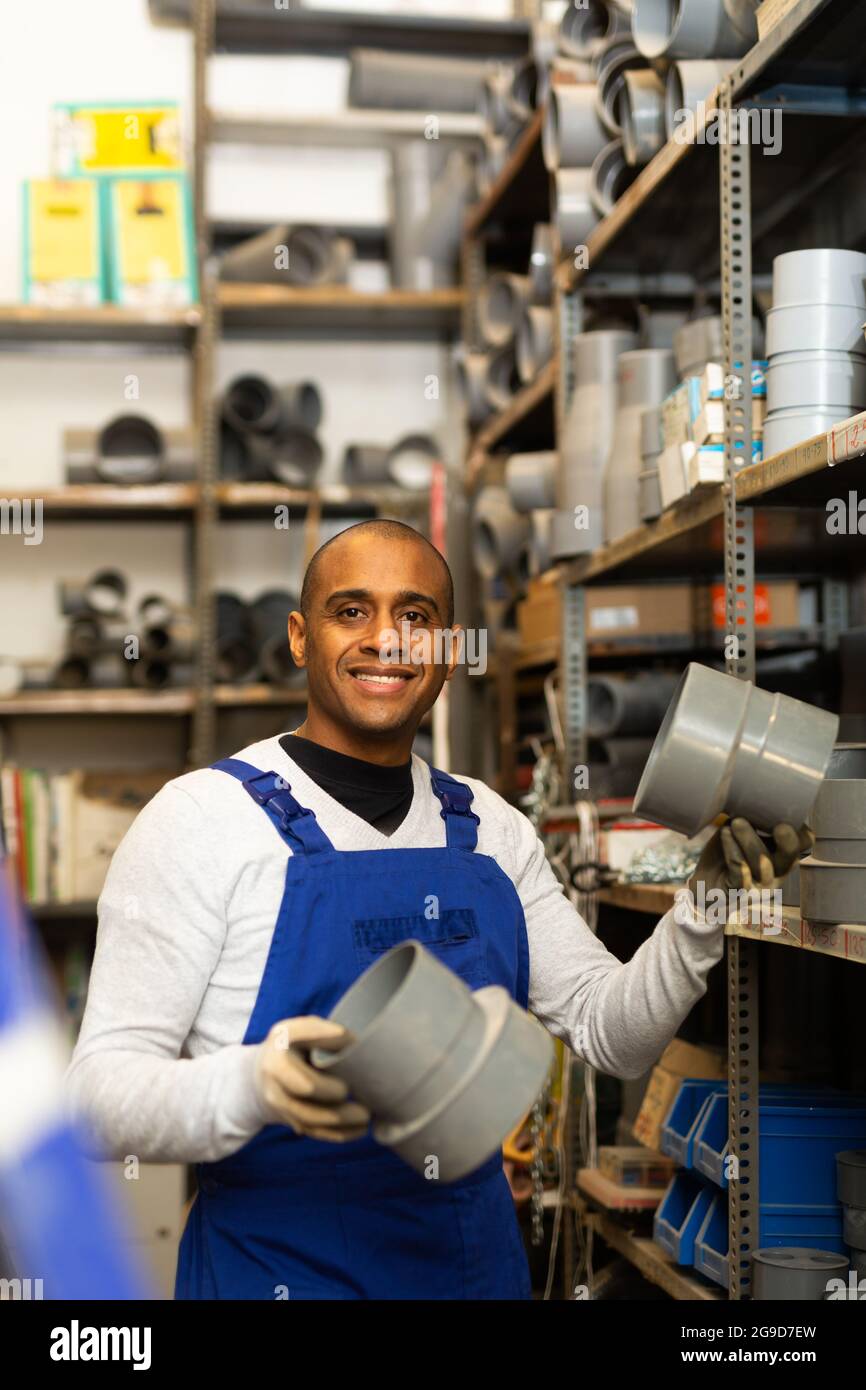 Worker in overalls lays out plumbing fittings on the shelves of ...