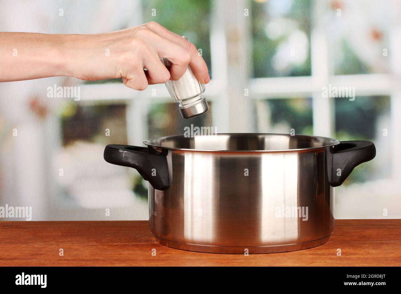 Hand adding salt using salt shaker on bright background Stock Photo - Alamy